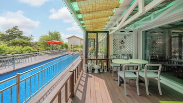 Uma área à beira da piscina com um deck de madeira, guarda-corpo de vidro e mobiliário de exterior.