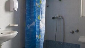 Área de chuveiro com cortina azul, chuveiro manual e torneira fixada na parede.