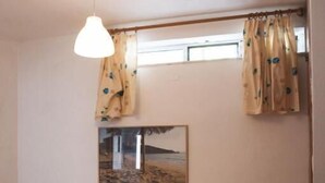 Quarto com duas camas de madeira, luminária pendente, janela com cortinas, pintura na parede e uma pequena mesa de cabeceira com uma planta.