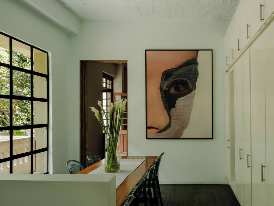 Um corredor com uma mesa de jantar, cadeiras, um vaso de flores e um quadro na parede.