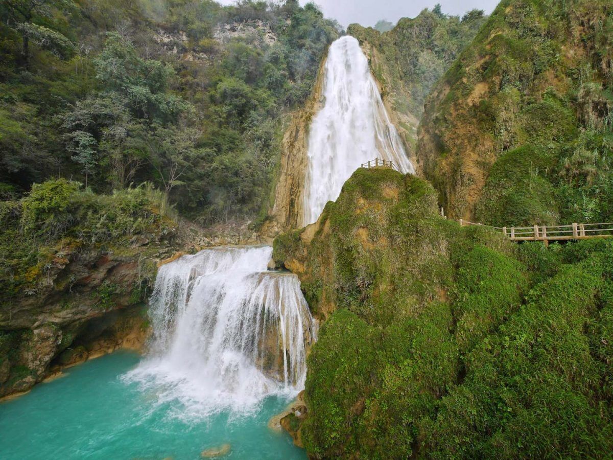 Uma cascata desce por um penhasco rochoso, rodeada por vegetação exuberante.