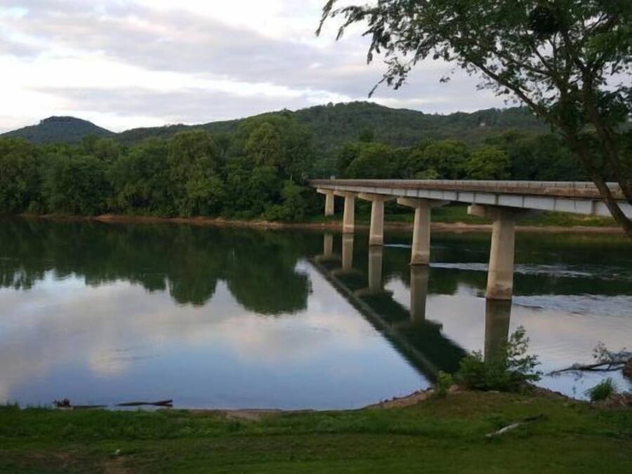 Um rio calmo com uma ponte e vegetação ao redor.
