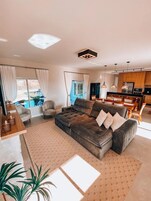 Uma sala de estar moderna com um amplo sofá modular, uma área de refeições e uma cozinha com armários de madeira e iluminação pendente.
