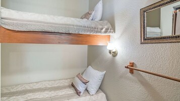 Uma cama de beliche com estrutura de madeira, uma mesa de cabeceira com abajur e um espelho na parede.
