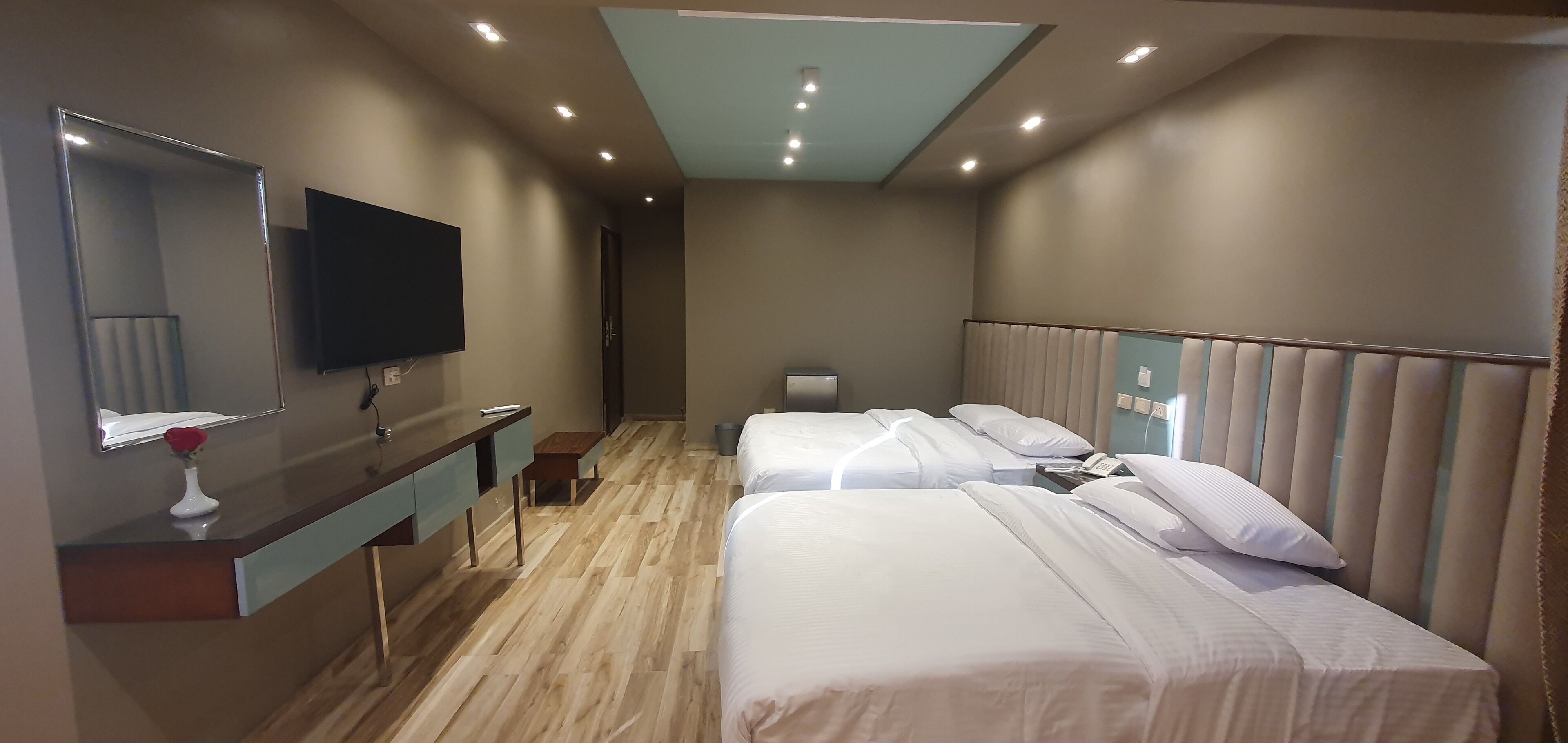 Quarto de hotel com duas camas, uma escrivaninha, um espelho, uma televisão e uma lâmpada no teto.