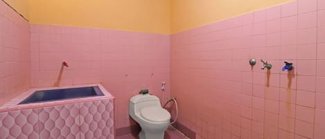 Um banheiro com paredes revestidas de azulejos rosa, vaso sanitário branco, banheira azul e área de chuveiro.