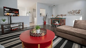 Uma sala de estar moderna com uma mesa de centro vermelha, um sofá marrom e uma TV de tela plana exibindo 'Stranger Things'.
