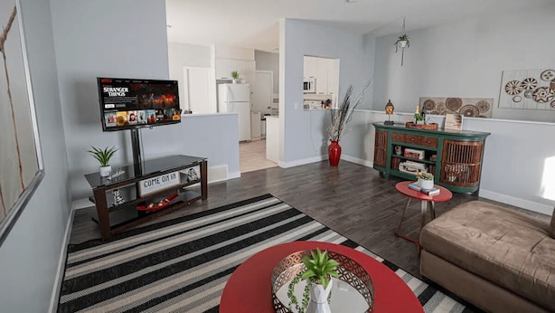 Uma sala de estar com televisão de tela plana, sofá, mesa de centro e uma parede vermelha de destaque.