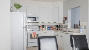 Cozinha moderna com armários brancos, micro-ondas e área de jantar com mesa posta para dois.