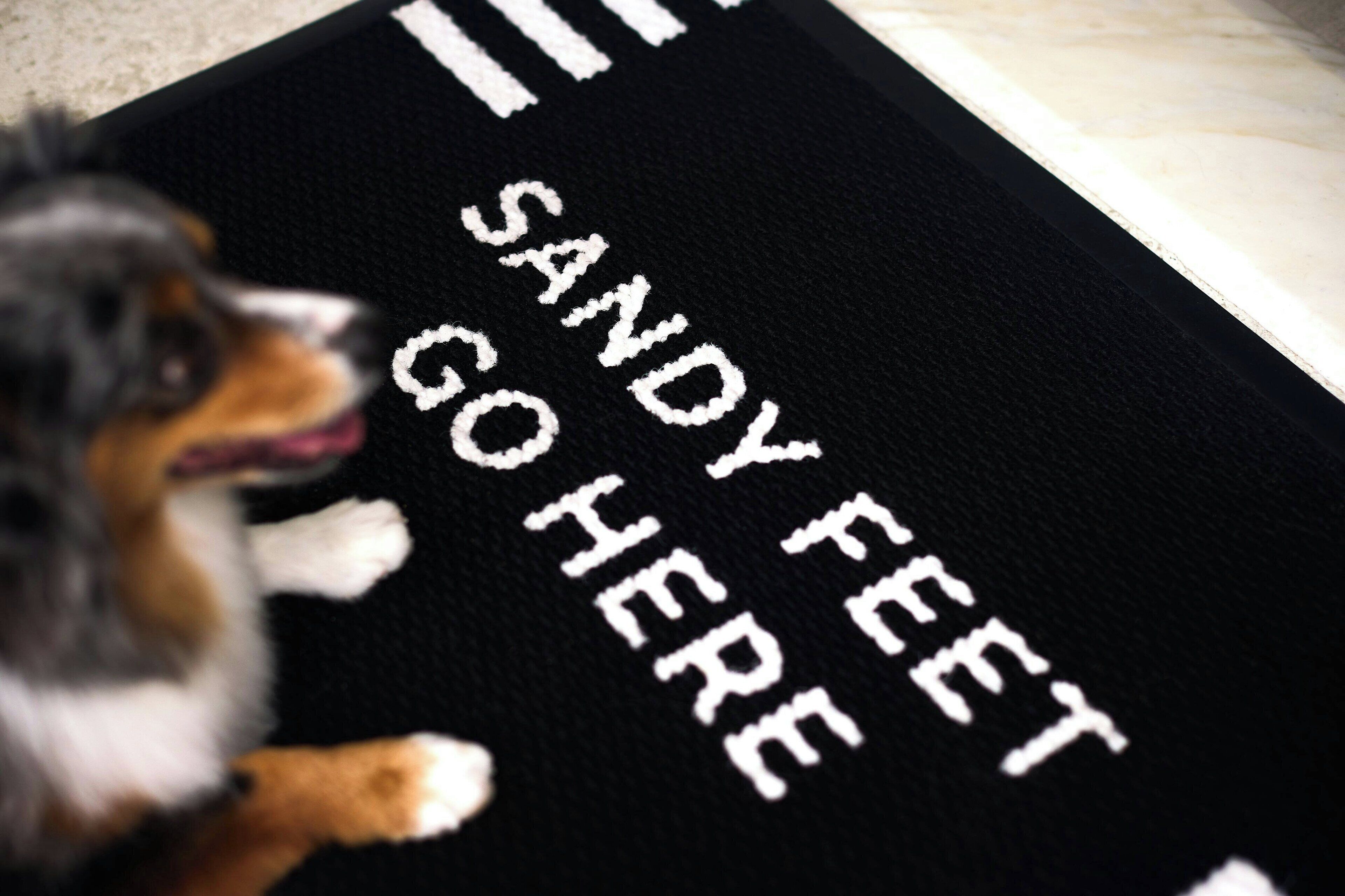 Um tapete preto com texto branco que diz 'SANDY FEET GO HERE'.