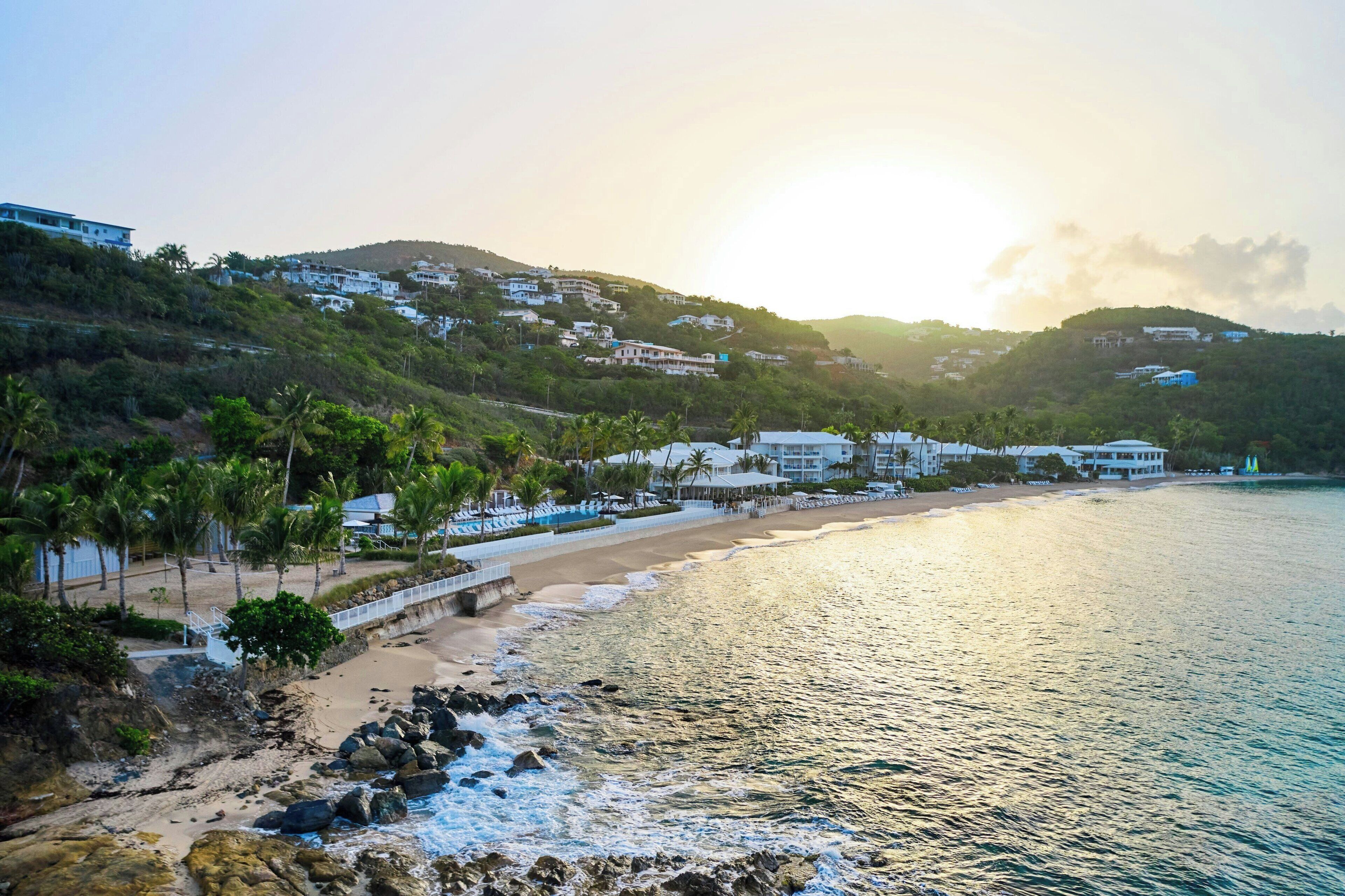 Um resort costeiro com villas na orla, uma praia de areia e um litoral rochoso.