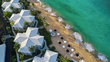Vista aérea de um resort com vários edifícios, uma praia e guarda-sóis ao longo da orla.