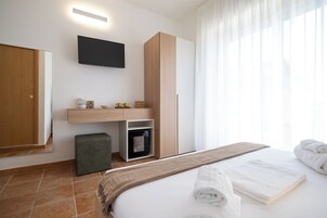 Quarto de hotel moderno com cama, televisão de tela plana na parede, guarda-roupa de madeira e um pequeno espaço de estar com cafeteira.