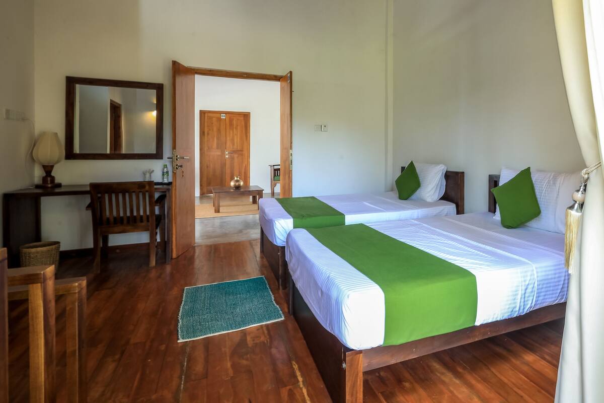 Quarto de hotel com duas camas, uma escrivaninha, uma cadeira e um espelho.