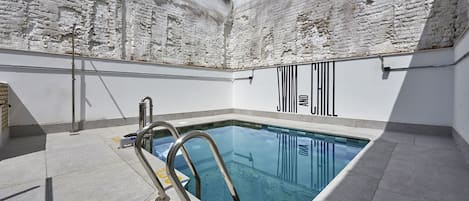 Piscina interior retangular com escada de metal, rodeada por paredes brancas e chão em azulejo.