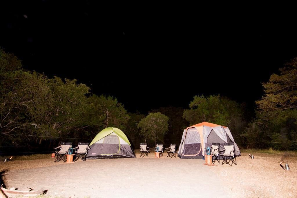 Um camping com duas barracas e várias cadeiras dispostas em fila.