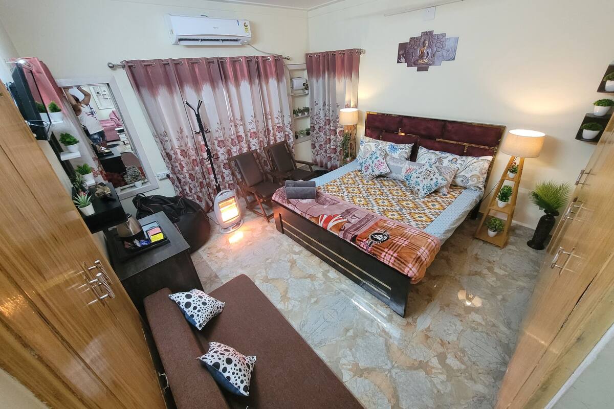 Um quarto com cama, escrivaninha, cadeira, sofá e luminária de chão.