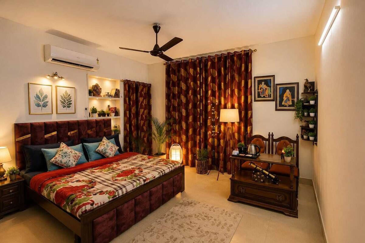 Quarto com cama, mesas de cabeceira, escrivaninha, cadeira, ventoinha no teto, cortinas, ar condicionado fixado na parede, obra de arte emoldurada e planta em vaso.