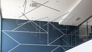 Um lobby moderno com design geométrico na parede, um sofá branco e uma escadaria de vidro.