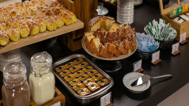 Mesa de buffet com diversos alimentos, incluindo doces, sobremesas e acompanhamentos.