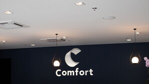 Uma área de recepção com parede escura e um letreiro que diz “Comfort”. Há três balcões de atendimento com design minimalista.