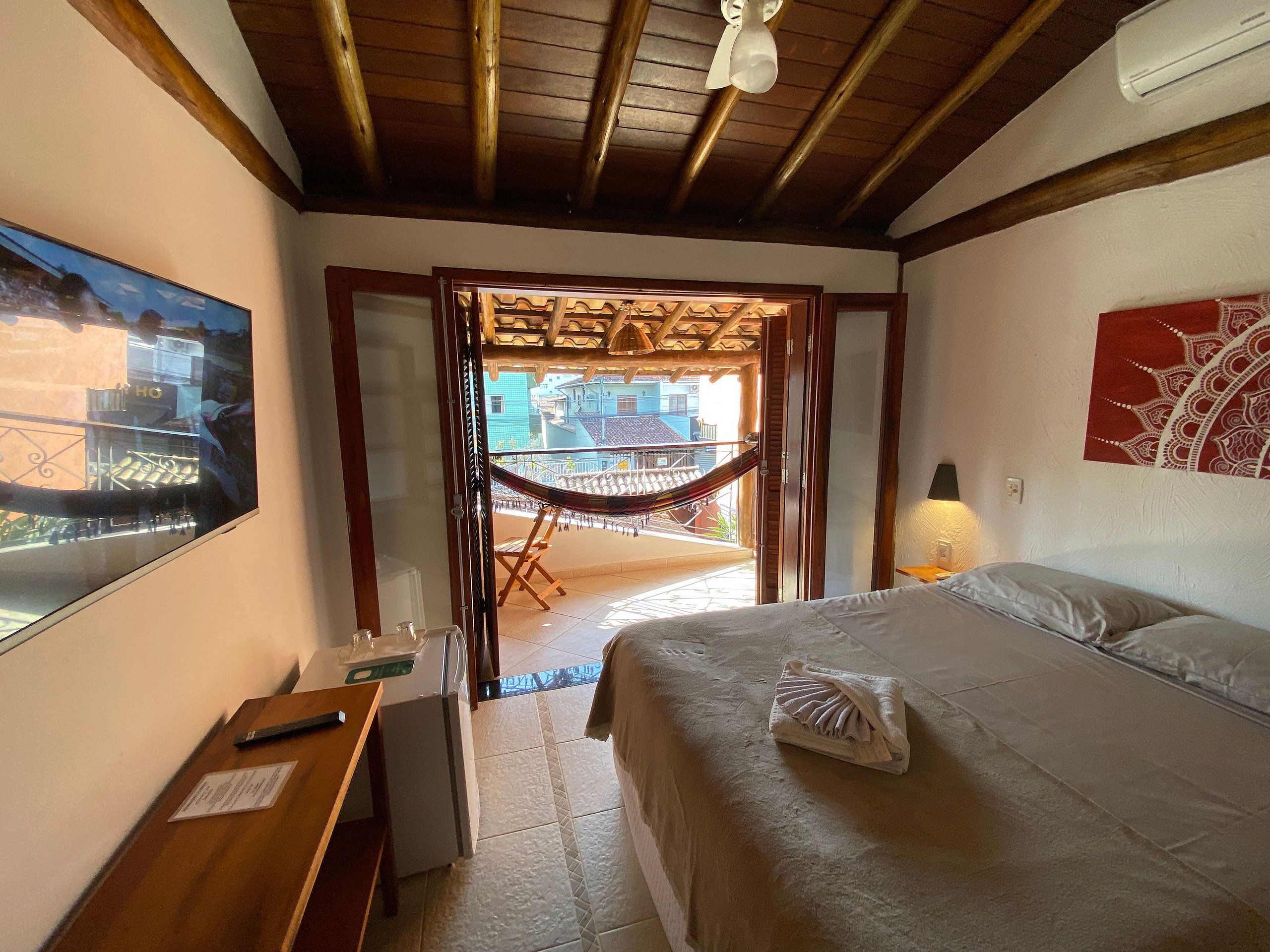 Quarto de hotel com cama, escrivaninha, cadeira, rede e vista para o exterior.