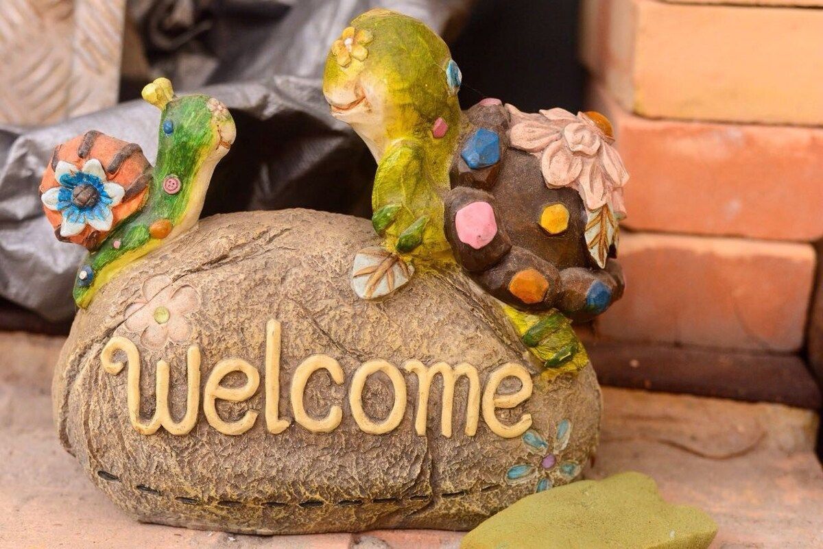 Uma rocha com a palavra 'Welcome' entalhada, rodeada por esculturas de pássaros coloridos.