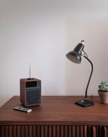 Uma secretária de madeira com um rádio antigo, uma luminária de mesa e um vaso com planta.
