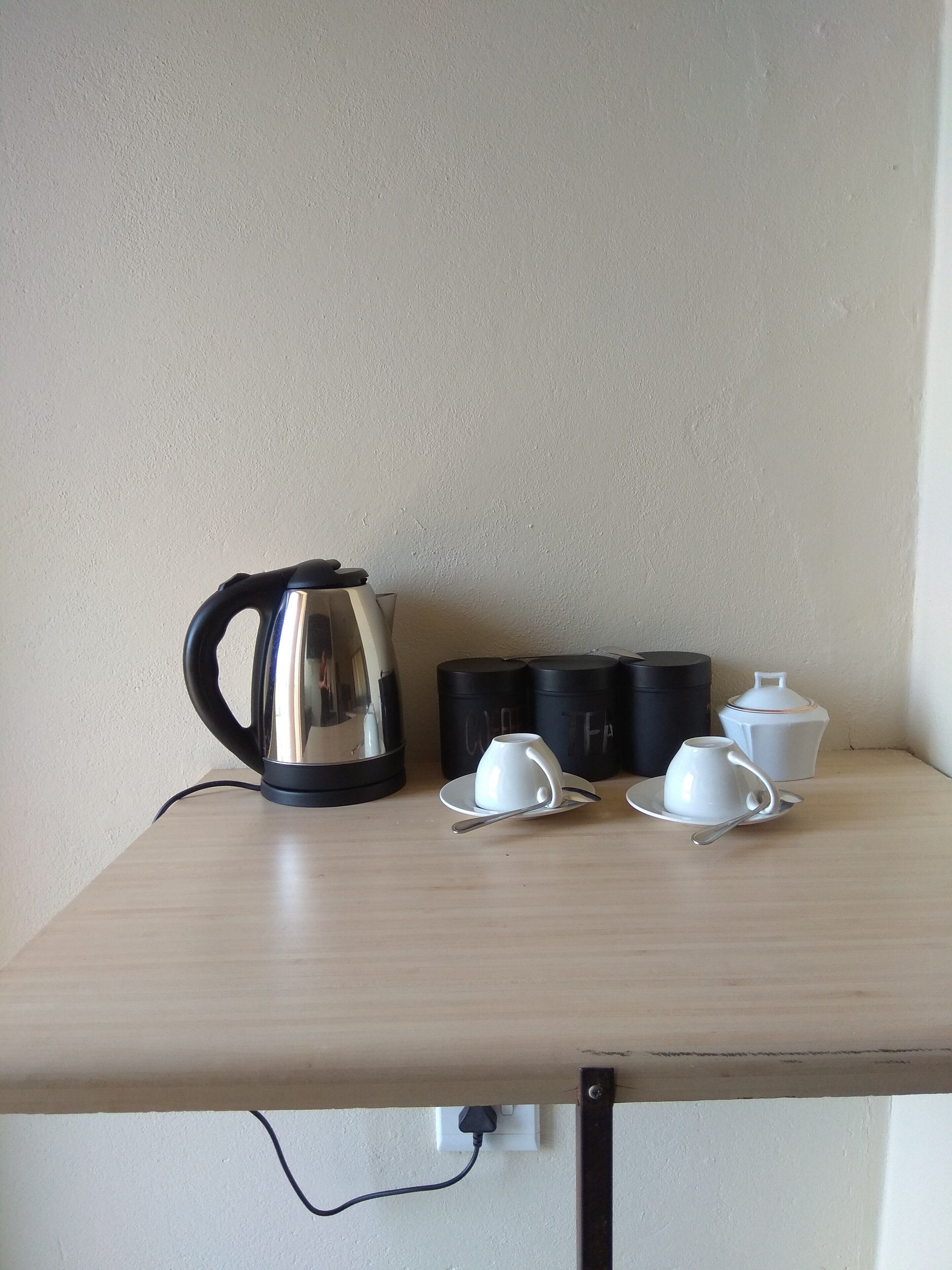 Uma cozinha compacta com uma chaleira, duas chávenas brancas e dois recipientes pretos sobre uma mesa de madeira.