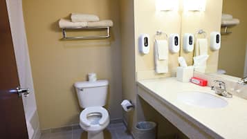 Casa de banho com sanita, lavatório e espelho. Inclui dispensadores de papel, secador de mãos e um contentor de lixo.
