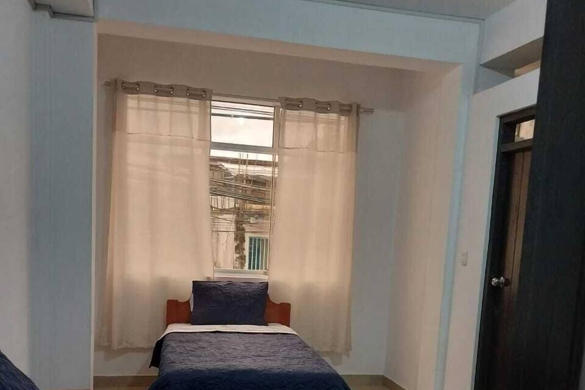 Quarto com duas camas, uma janela com cortinas e uma porta.