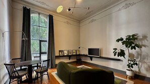 Uma sala de estar moderna com área de jantar, uma janela grande com cortinas, uma televisão de tela plana e um vaso de planta.