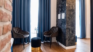 Quarto moderno com duas cadeiras escuras, uma mesinha redonda com duas garrafas e um pilar preto.