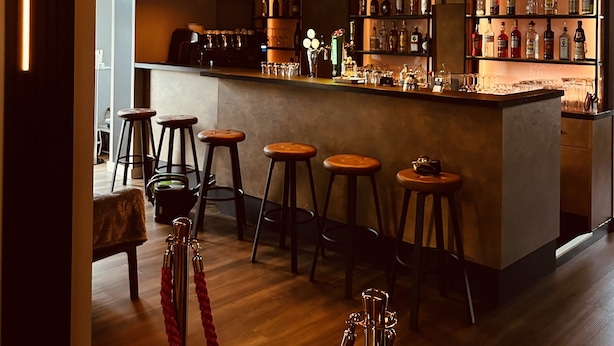 Uma área de bar com banquetas, um balcão e prateleiras cheias de garrafas.