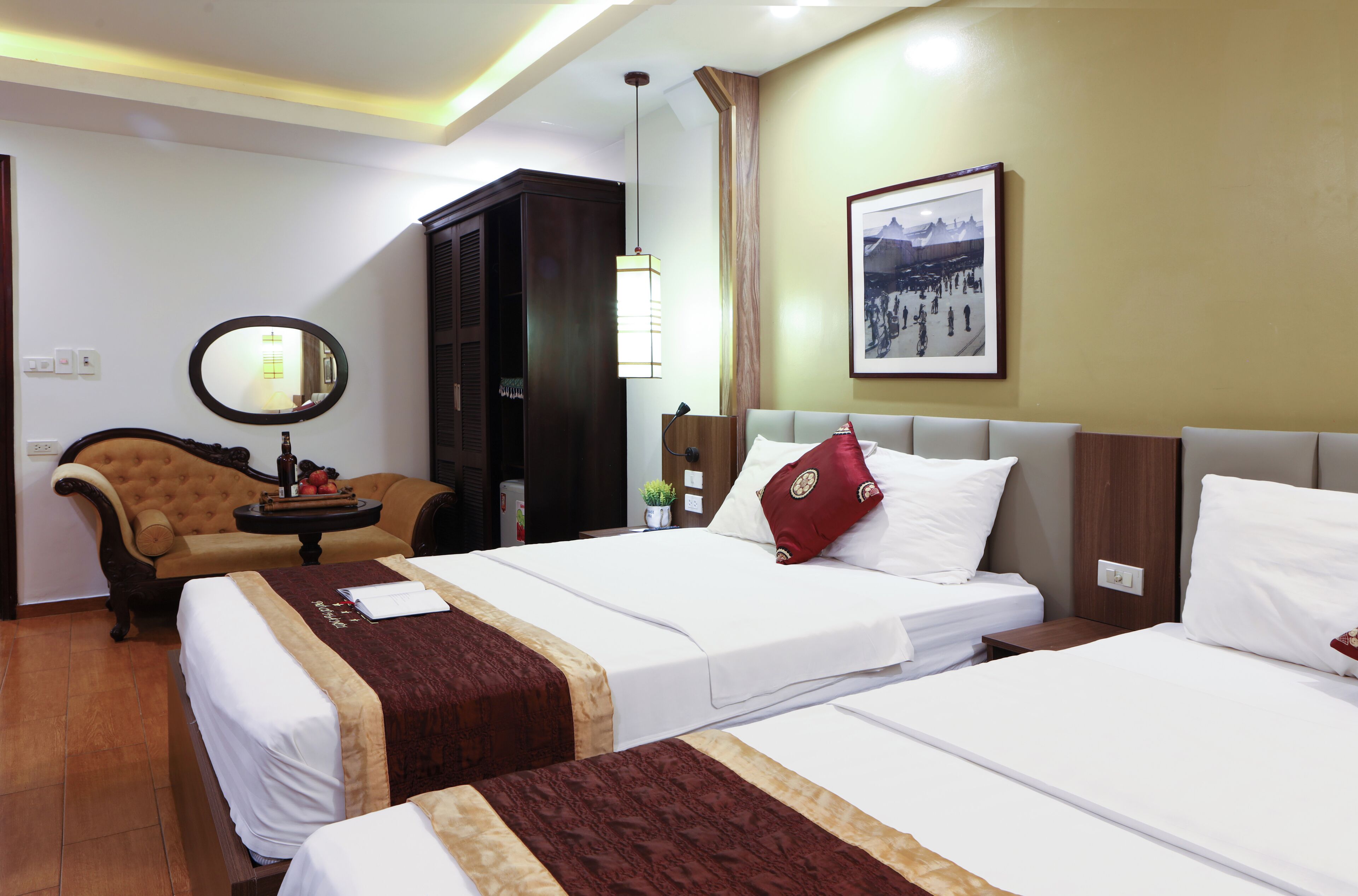 Quarto de hotel com duas camas, um espaço de estar com uma poltrona, um guarda-roupa e um quadro na parede.