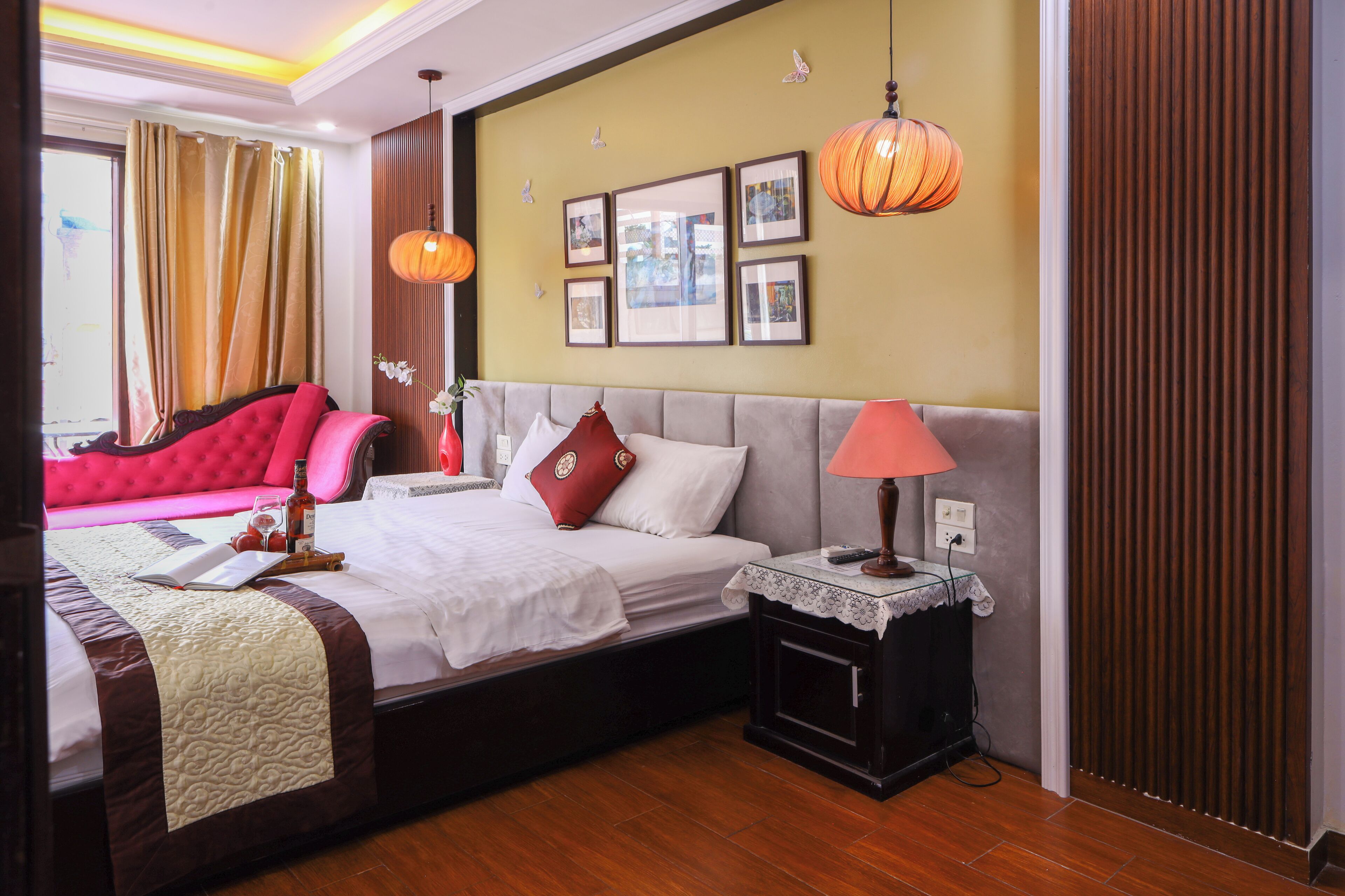 Quarto de hotel com uma cama grande, uma mesa de cabeceira e uma parede com quadros.