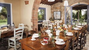 Uma área de refeições com um arco de tijolos rústicos, vigas de madeira e uma mesa grande posta para uma refeição.