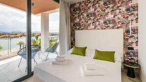 Quarto de hotel com uma cama grande, duas almofadas verdes e vista para a paisagem urbana e a água.