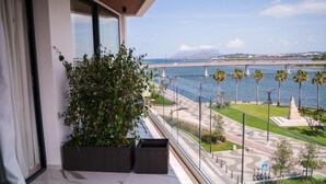 Uma varanda com vista para um calçadão à beira-mar, palmeiras e uma ponte.