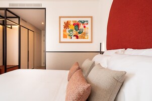 Quarto de hotel com cama, almofadas, uma obra de arte abstrata emoldurada na parede e uma porta deslizante que dá para um closet espaçoso.