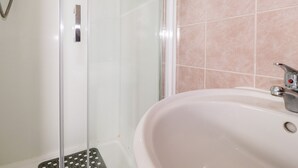 Casa de banho com cabine de duche, lavatório e parede revestida a azulejos.