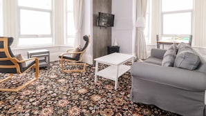 Quarto de hotel com sofá, poltrona, mesinha e televisão na parede.
