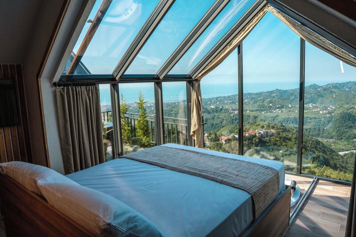 Quarto com um amplo claraboia, uma cama e vista para uma paisagem acidentada.