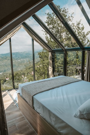 Quarto com um amplo claraboia, cama de madeira e vista para uma paisagem montanhosa.