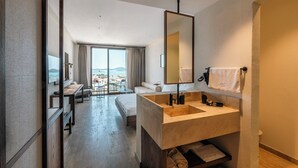 Quarto de hotel moderno com uma janela grande, uma penteadeira de madeira, um sofá e um espaço de jantar.