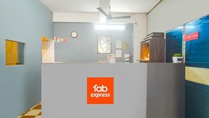 Uma área de recepção com um balcão cinza, um relógio e um ventilador de teto.