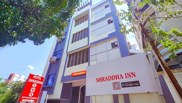 Um hotel chamado Shraddha Inn, com uma placa anunciando quartos com ar condicionado e um código QR do Google Maps.
