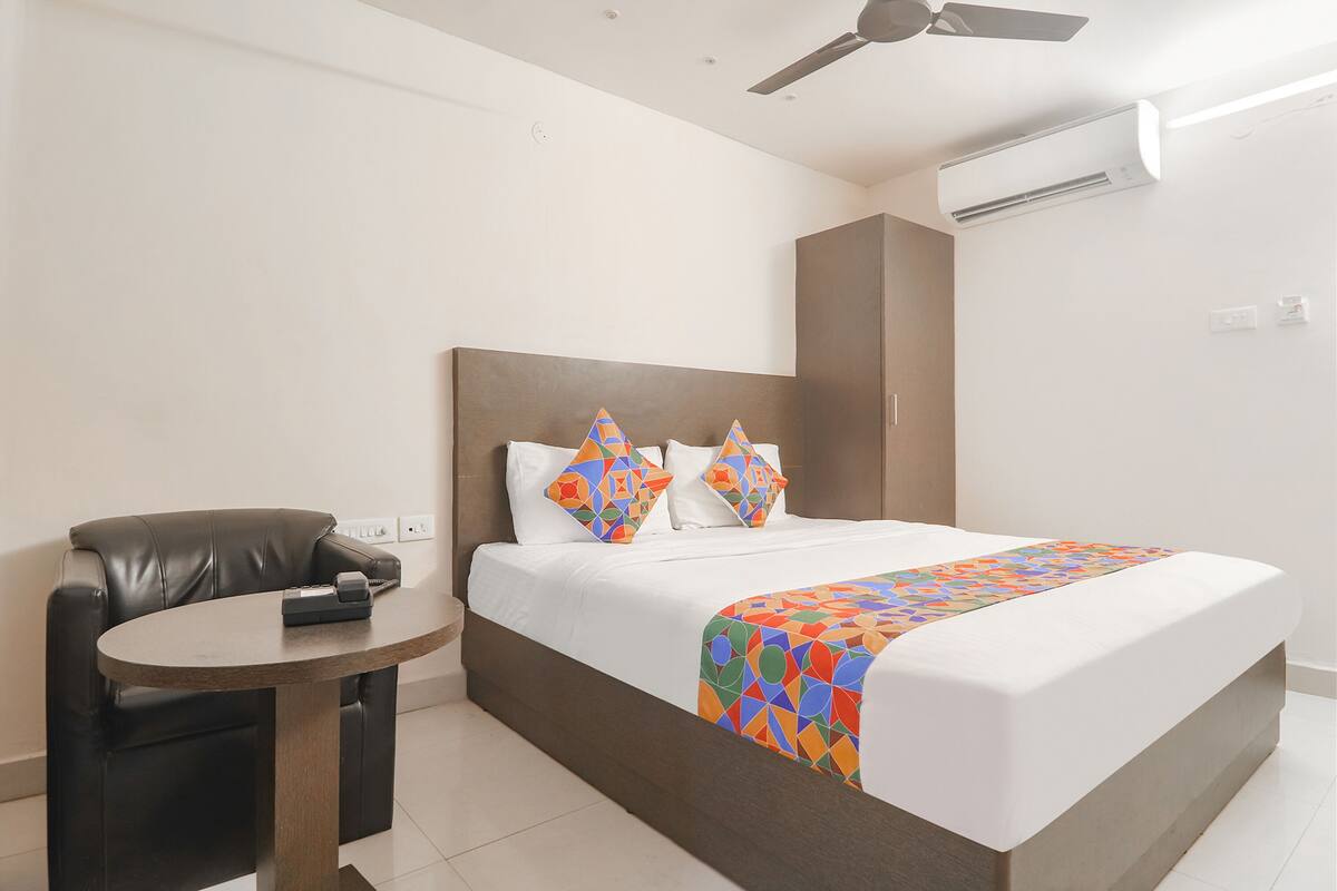 Quarto de hotel com cama, uma mesinha redonda, uma cadeira e ventoinha no teto.