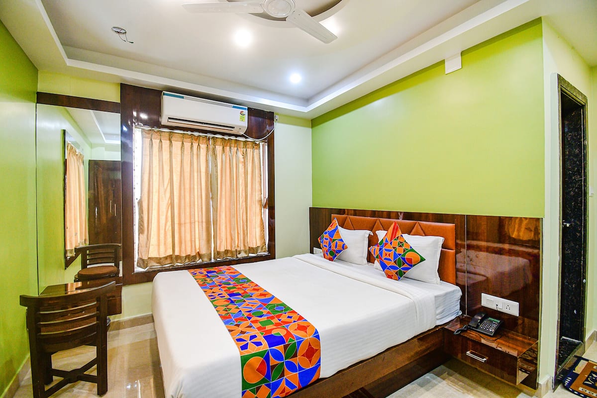 Quarto de hotel com cama, escrivaninha, cadeira, telefone e janela com cortinas.