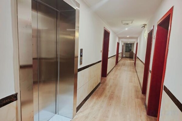 Um corredor comprido e estreito, com um elevador central e portas em ambos os lados, e piso de madeira.